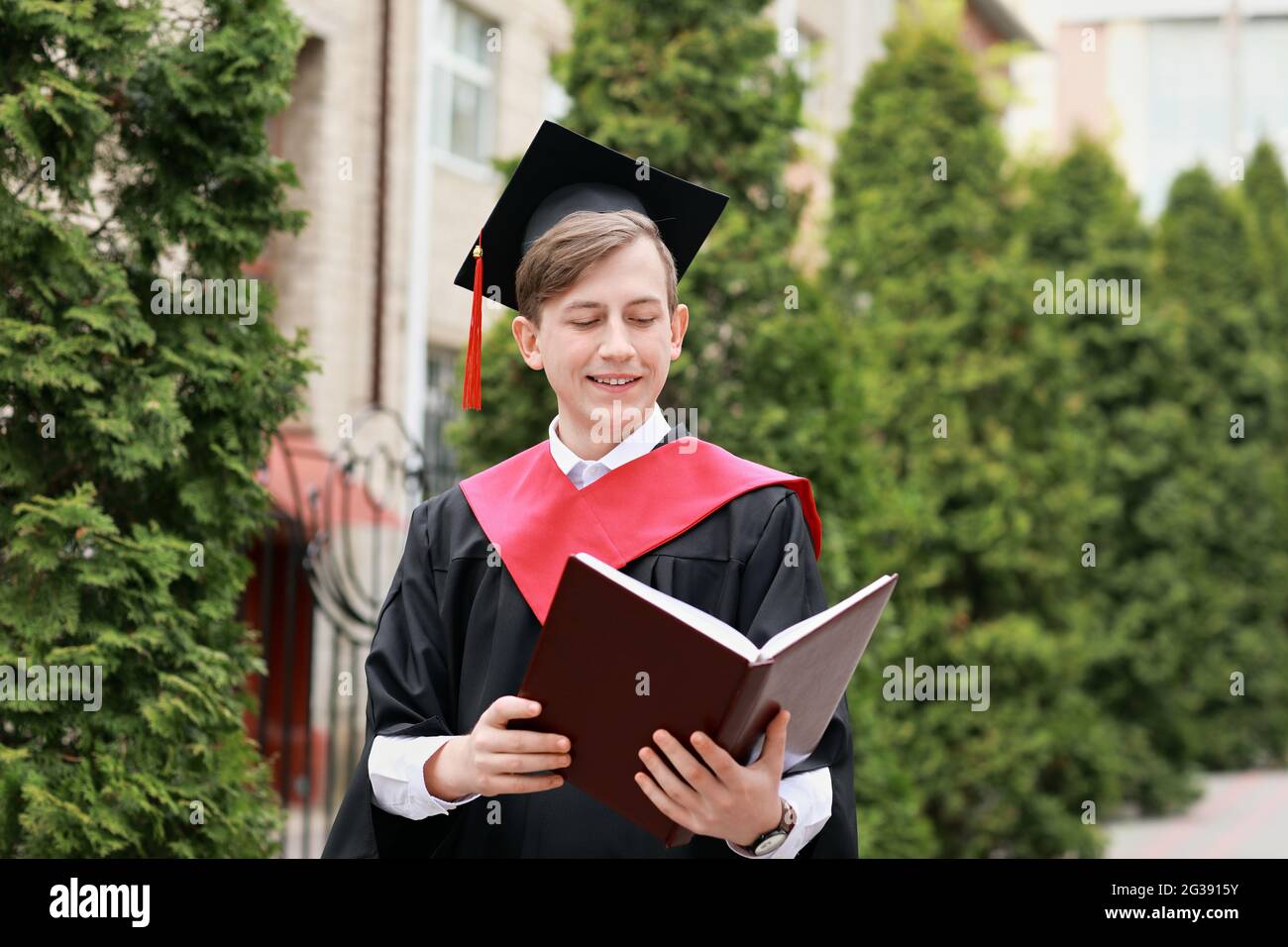 Portrait of male graduating student with book outdoors Stock Photo - Alamy