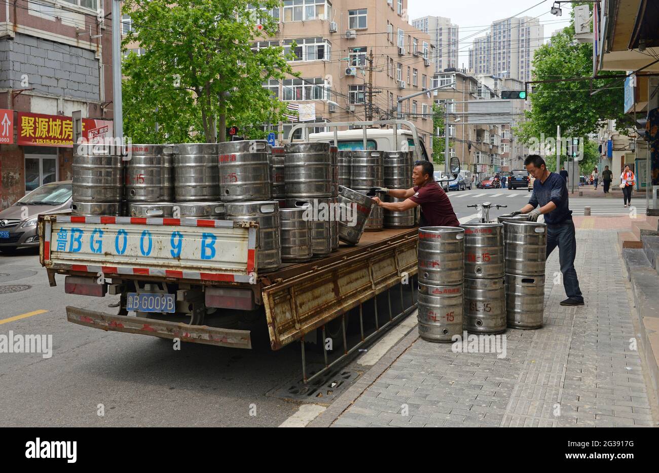 Two men deliver casks of Tsingtao beer to a bar in a street in Qingdao ...