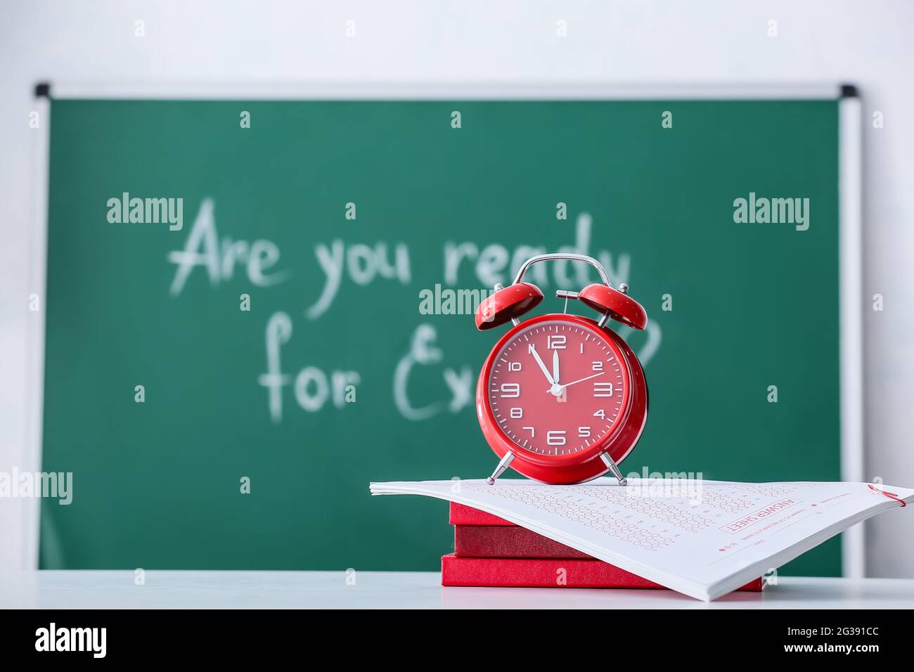 Stack of books and answer sheet forms with alarm clock on table in ...