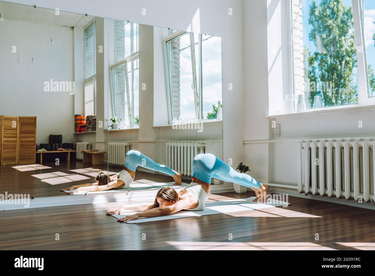 Young female do complex of stretching yoga exercises on floor in light ...