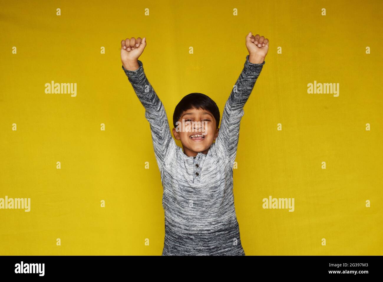 Cute little Indian boy raising hands and smiling against a yellow ...