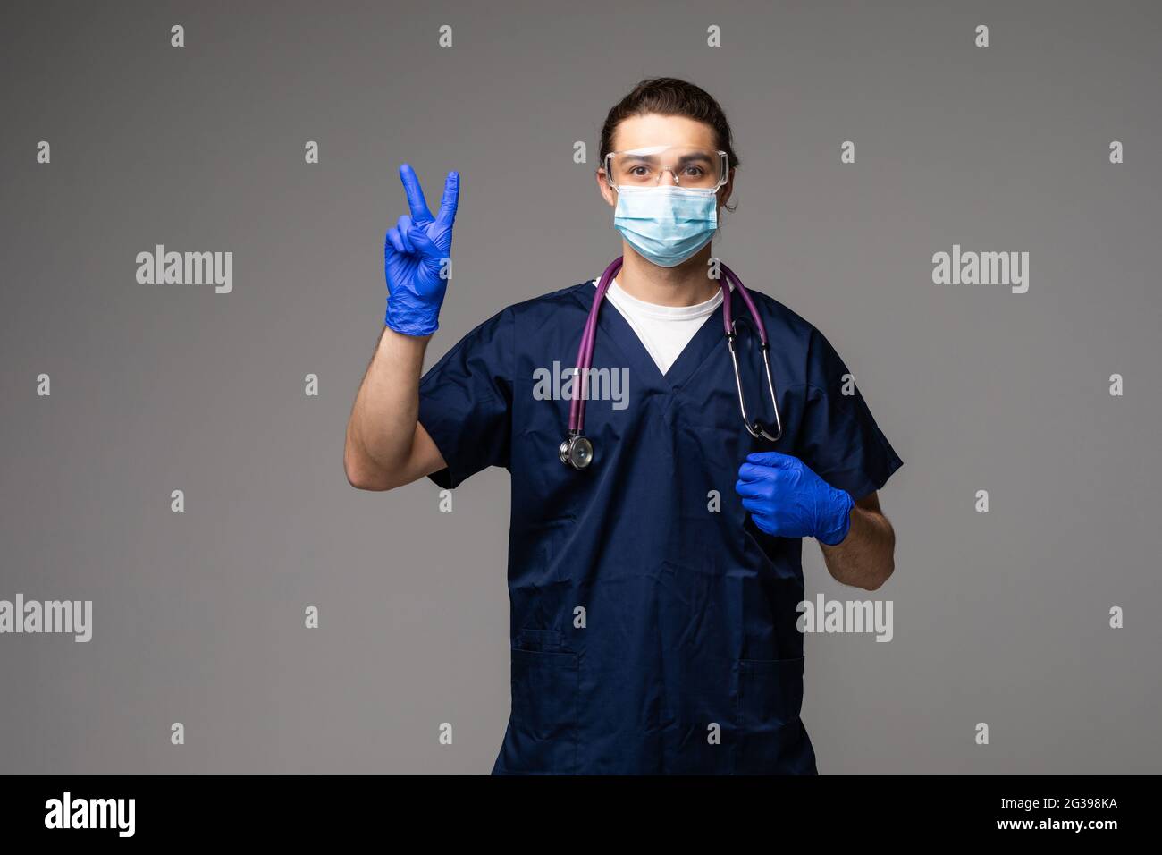 Portrait of smiling doctor showing peace sign or number two with his ...