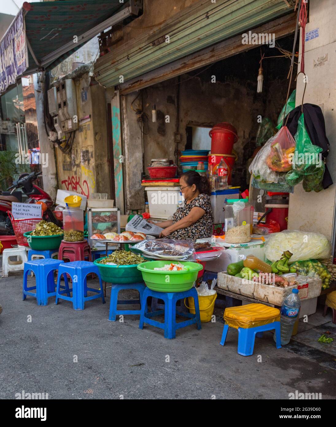 A fruit and veg street merchant reading a newspaper outside her store ...
