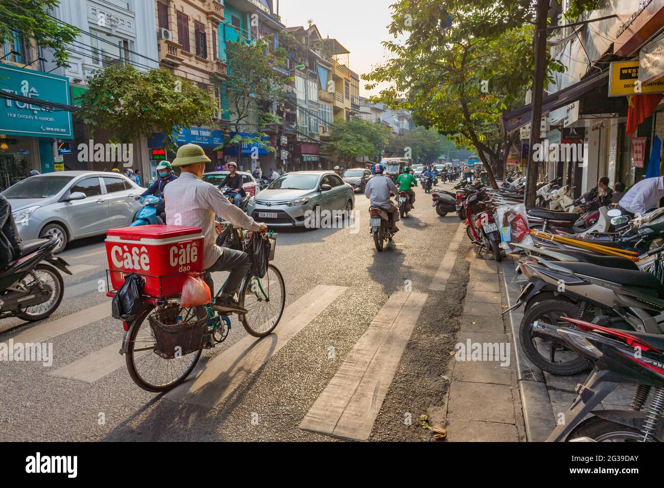 A cyclist on a bike carrying a storage box along a budy street in Hanoi ...