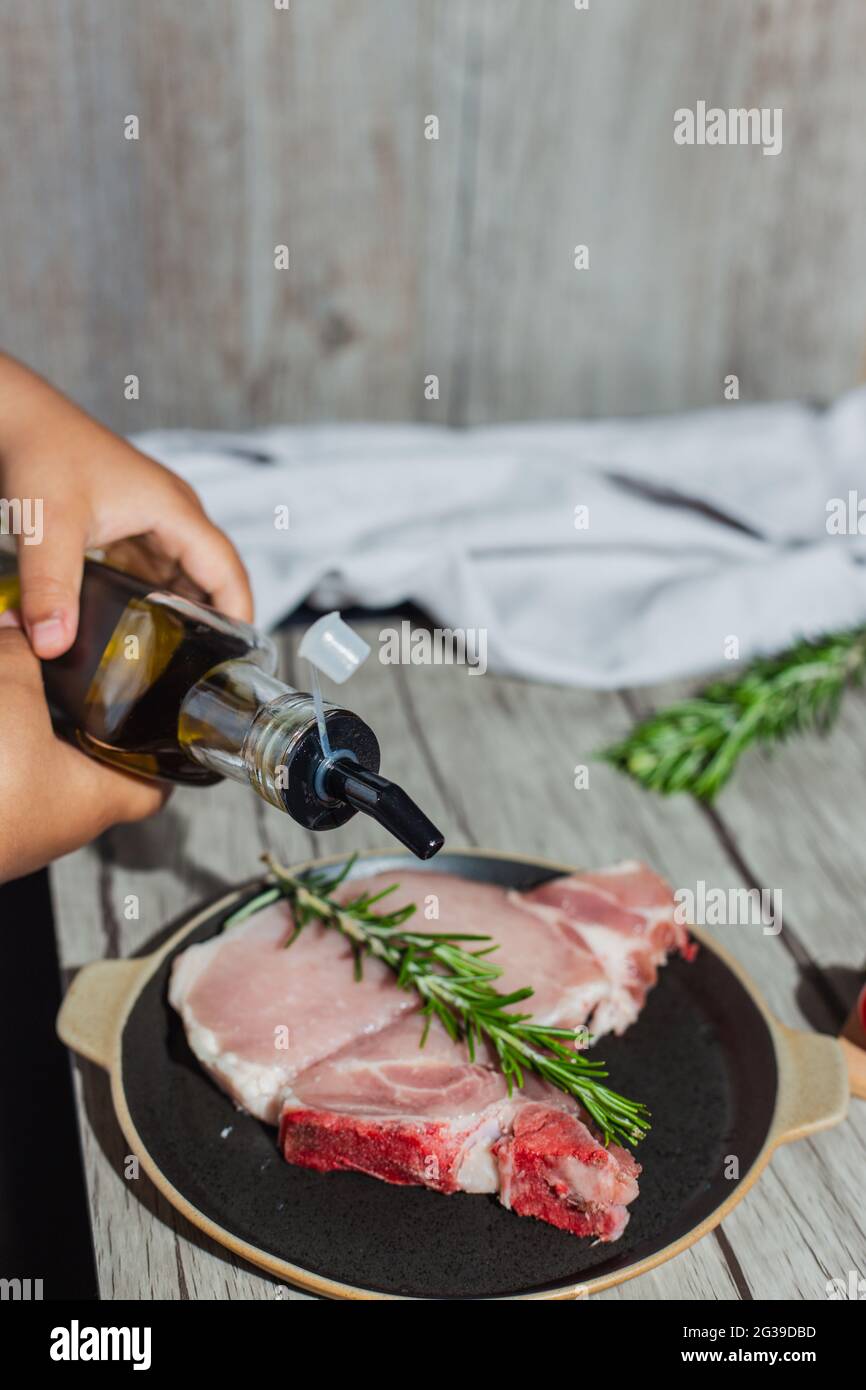 Vertical shot of a cook making pork steak with olive oil and rosemary ...