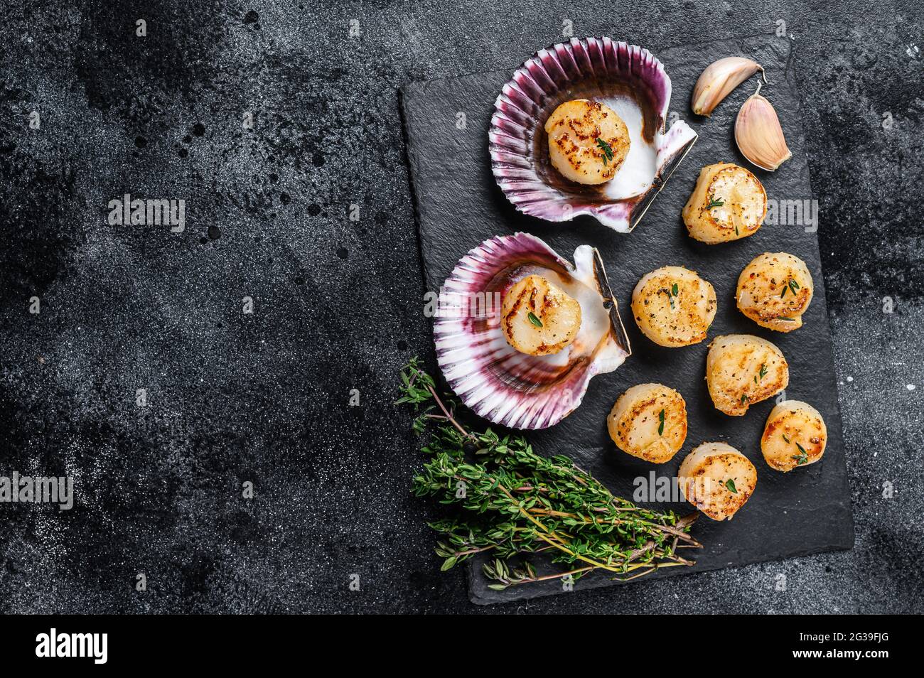 Fried seafood scallops meat with butter in a shells. Black background ...