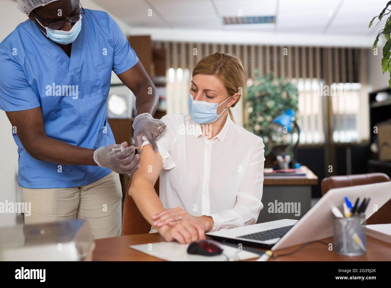 Qualified health worker vaccinates a young female employee in a ...