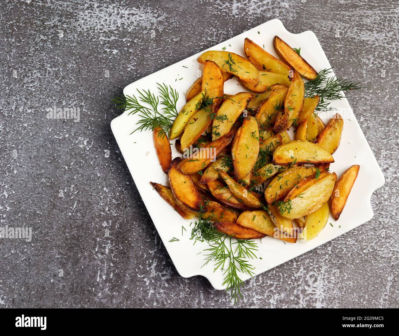 Fried potatoes with herbs on a white rectangular plate on a dark ...