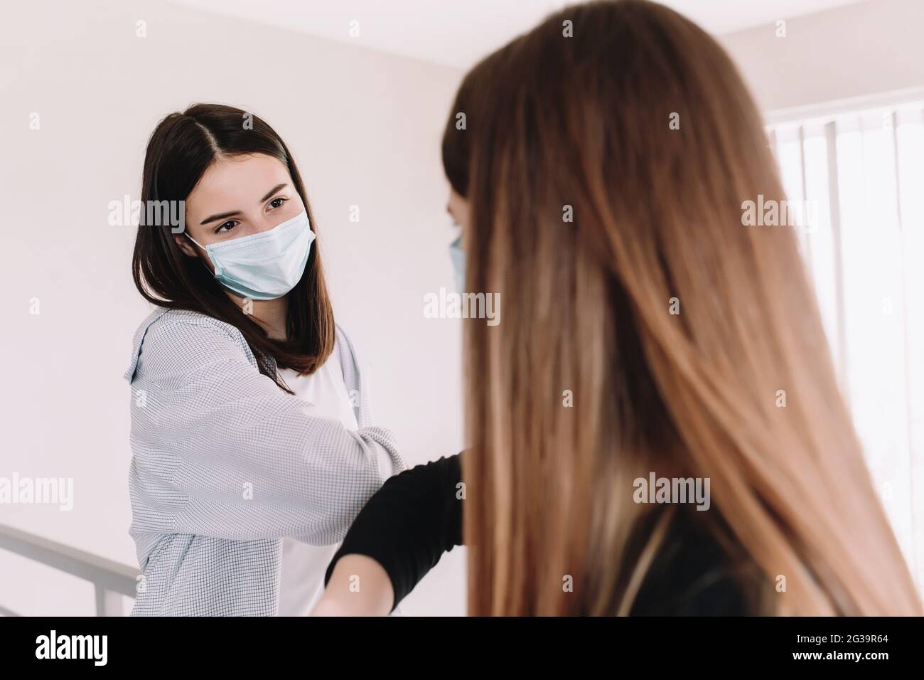 Two smiling girls in protective face mask say hello in safe way with ...