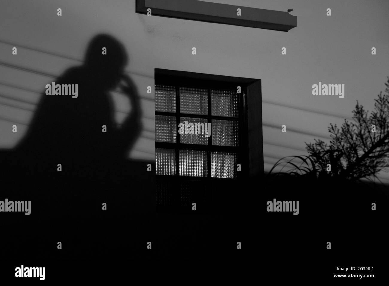 Shadow of a thoughtful man smoking on a white wall next to a window ...