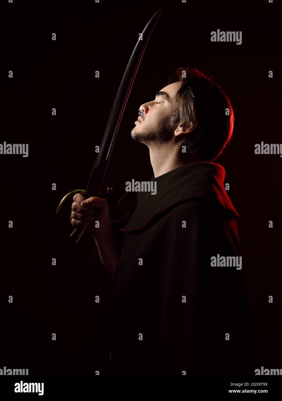 Profile, portrait of adult man in cape standing sideways holding sabre ...