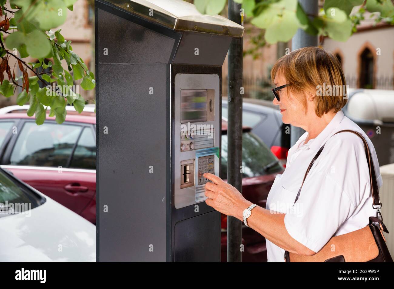 Smiling middle aged woman using parking machine to pay for car parking ...