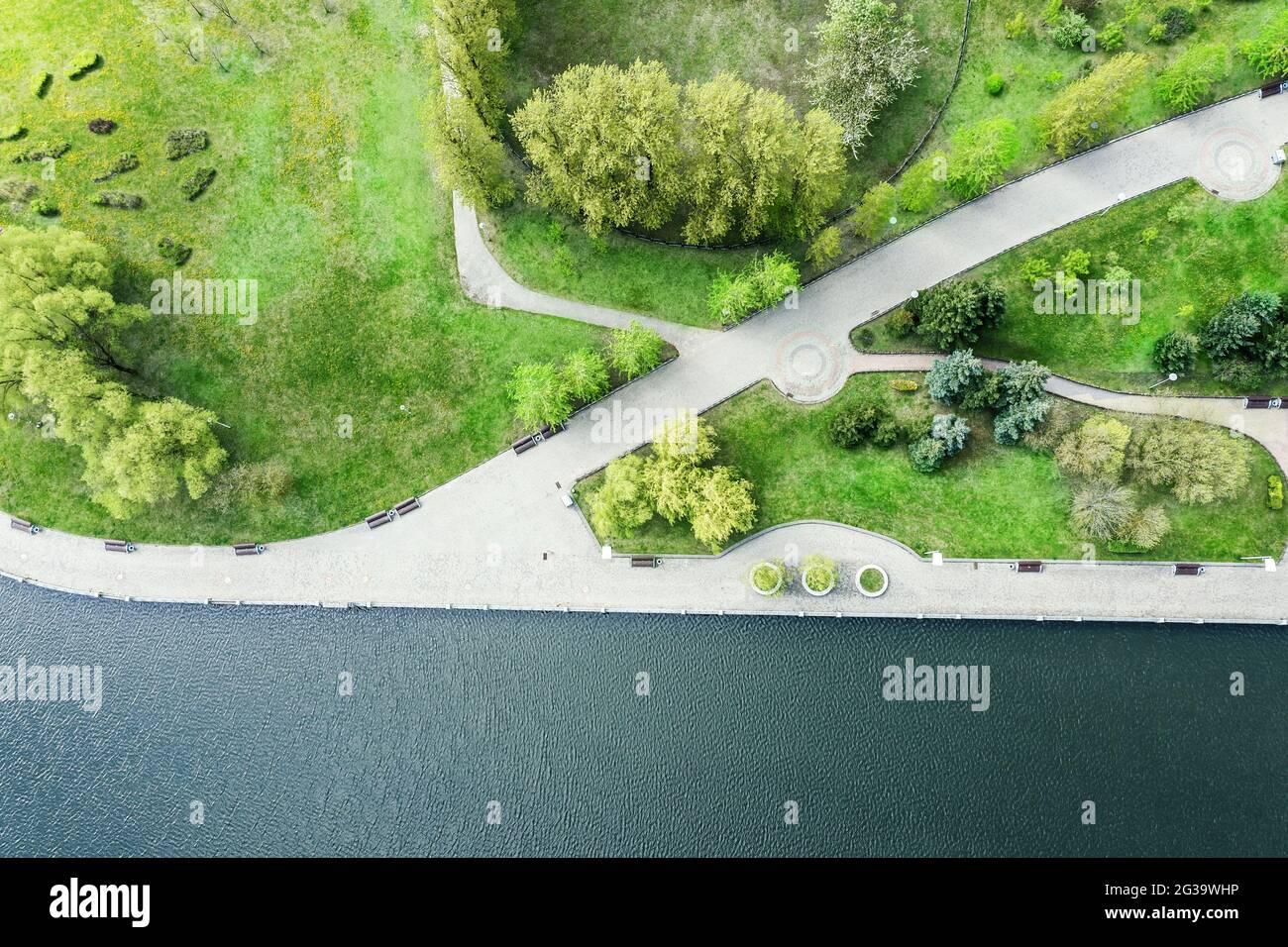 aerial top view of green park on river shore with footpaths and trees ...