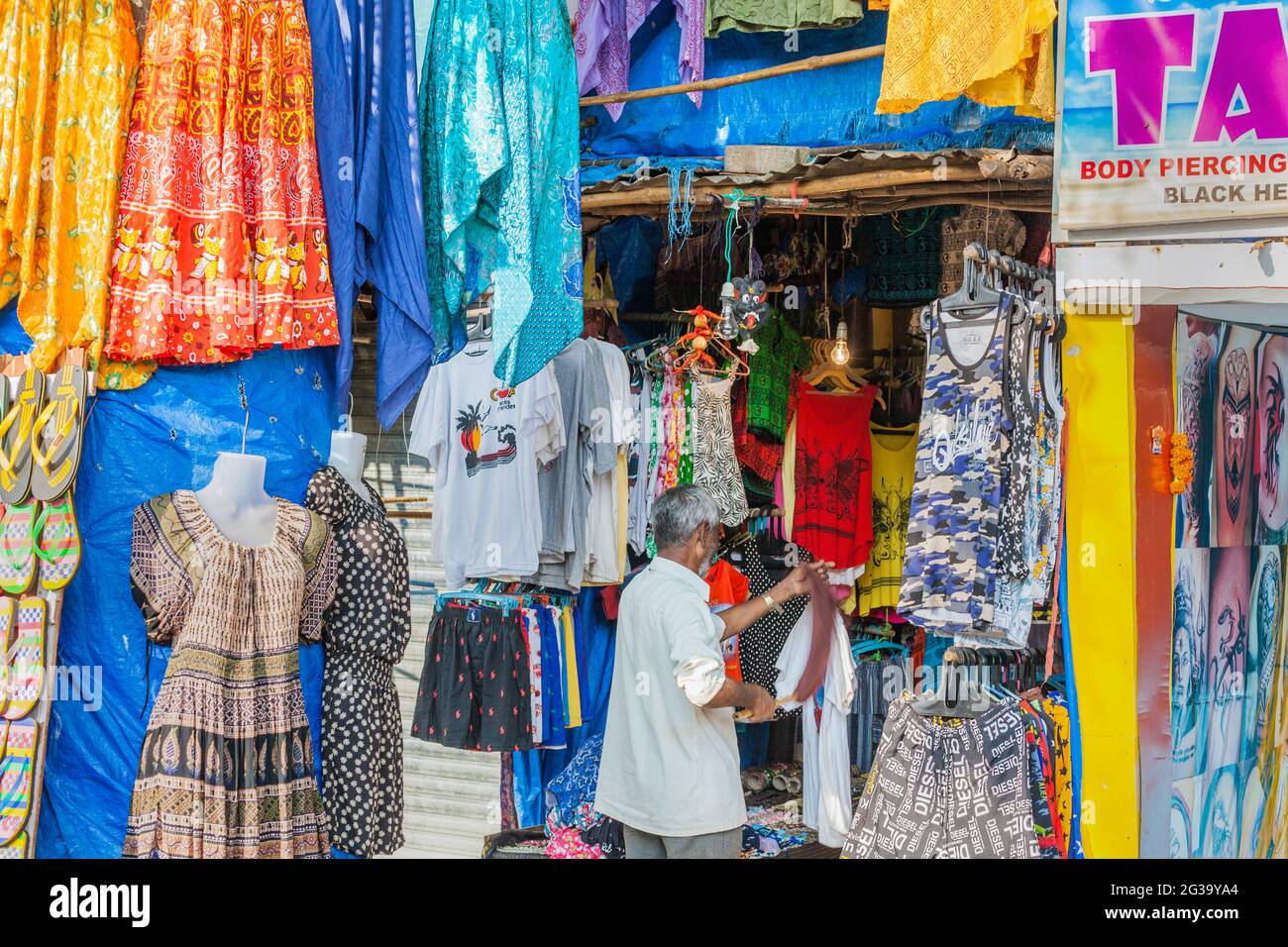 Indian trader dusts the clothing on his colourful clothing stall ...