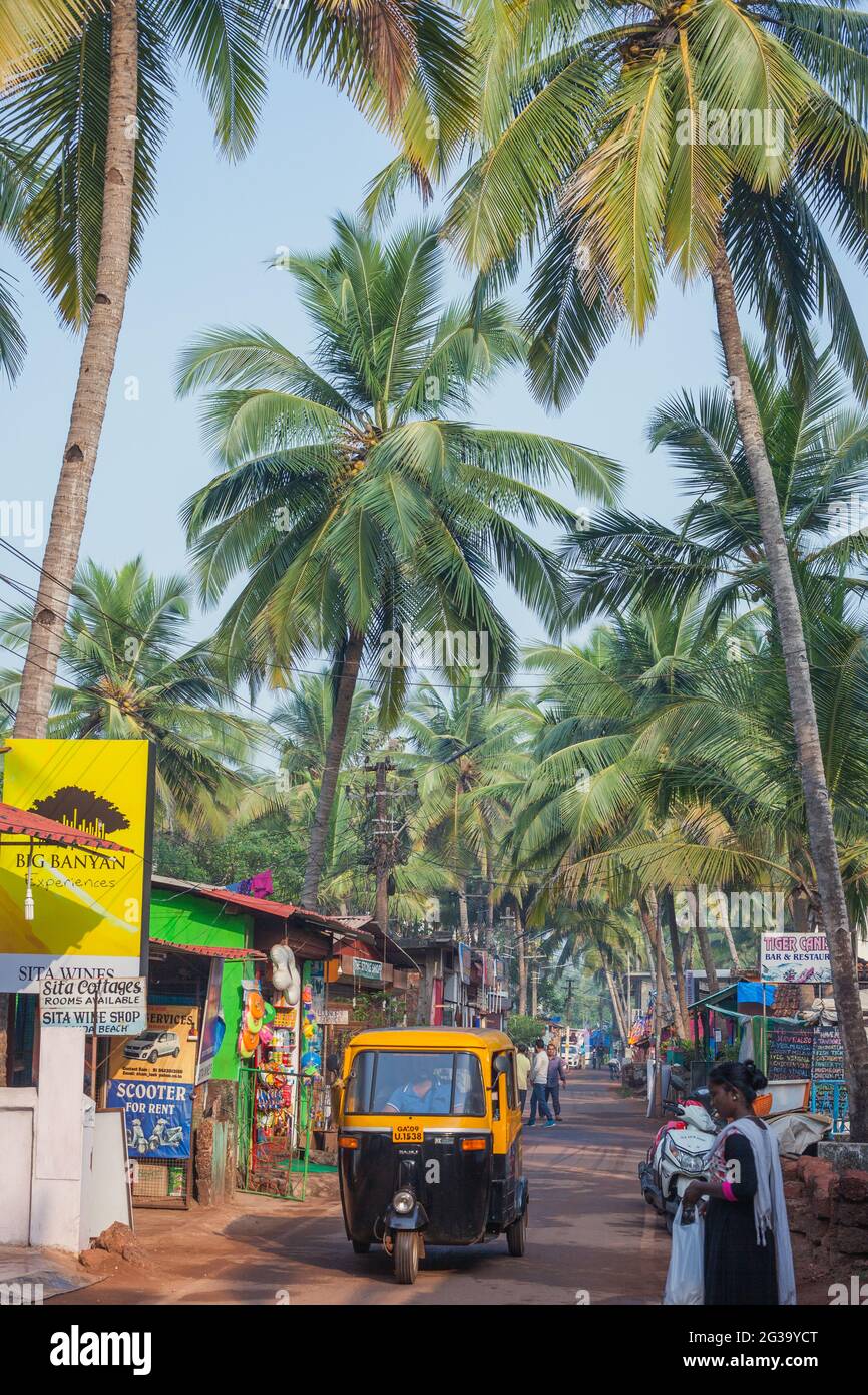 Auto Rickshaw driving along colourful Agonda Beach Road with palm trees ...