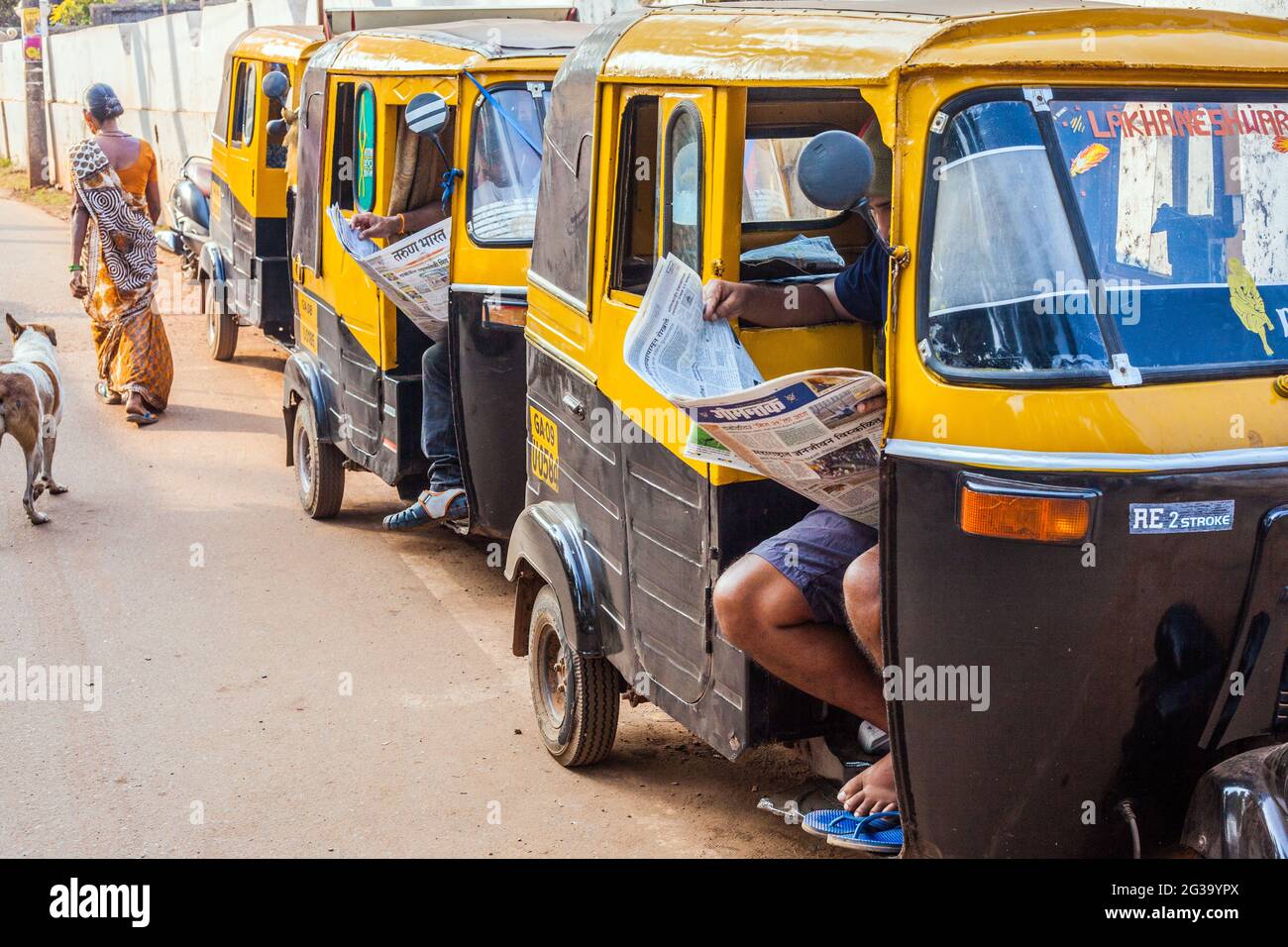 Two Indian auto rickshaw drivers sat in their separate vehicles reading ...
