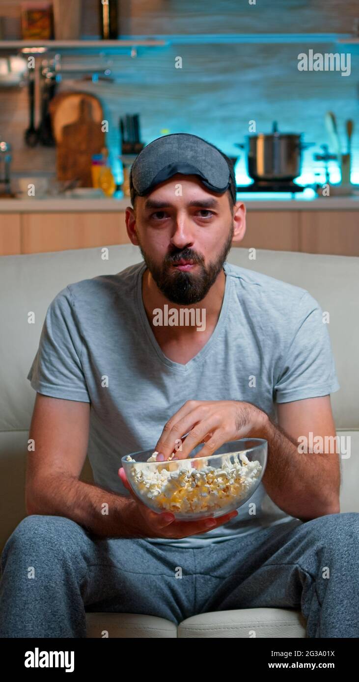 Portrait of man with beard holding popcorn bowl while watching entertainment movie on television ...