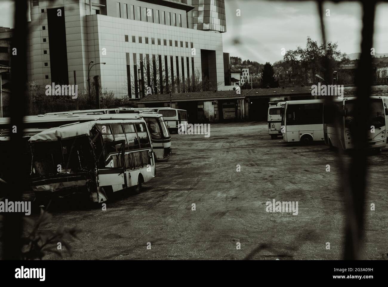 Grayscale shot of old, destroyed school buses outside of an old school ...