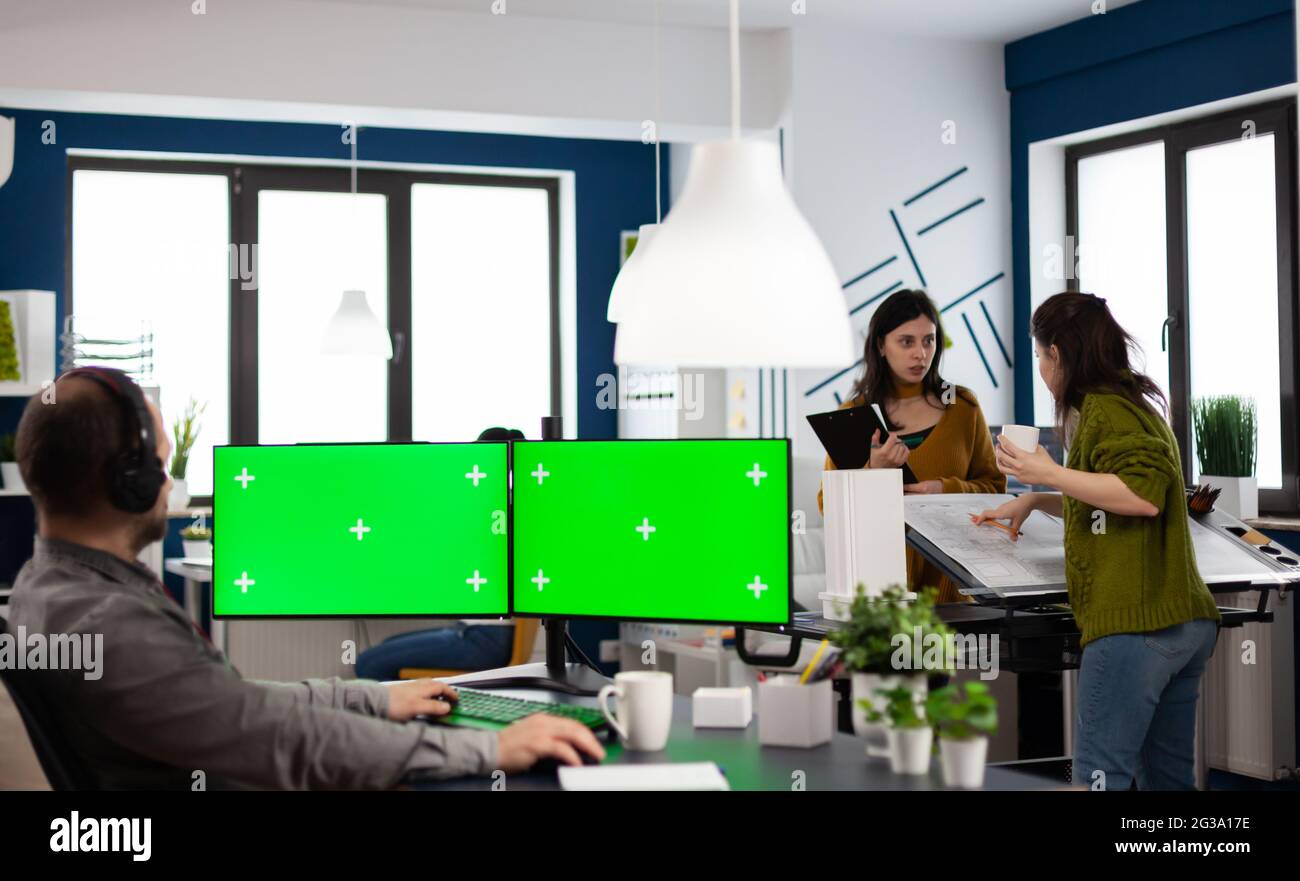 Employee with headphones using dual monitror setup with green screen ...