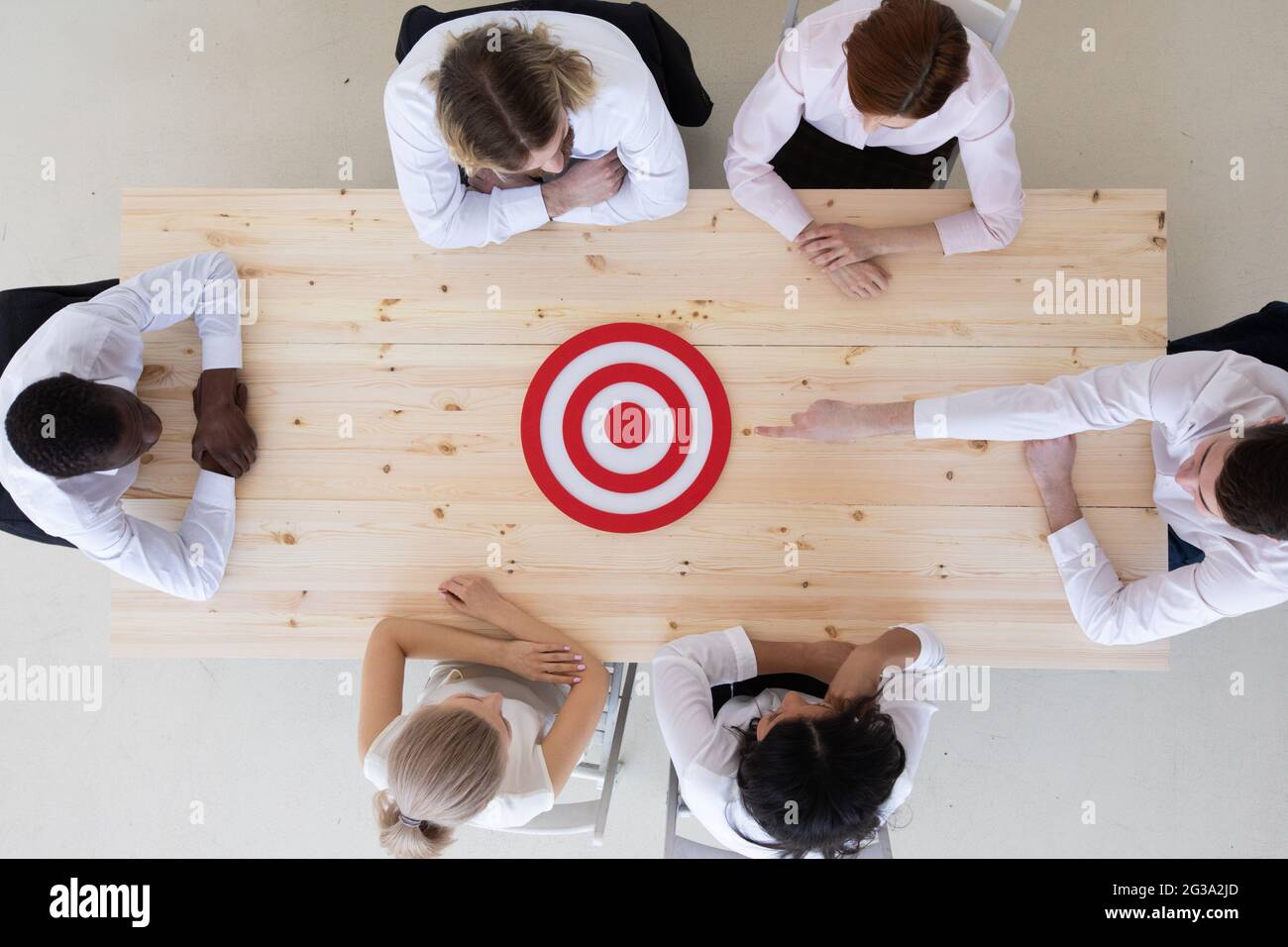 Team of business people pointing at red goal target at meeting table ...