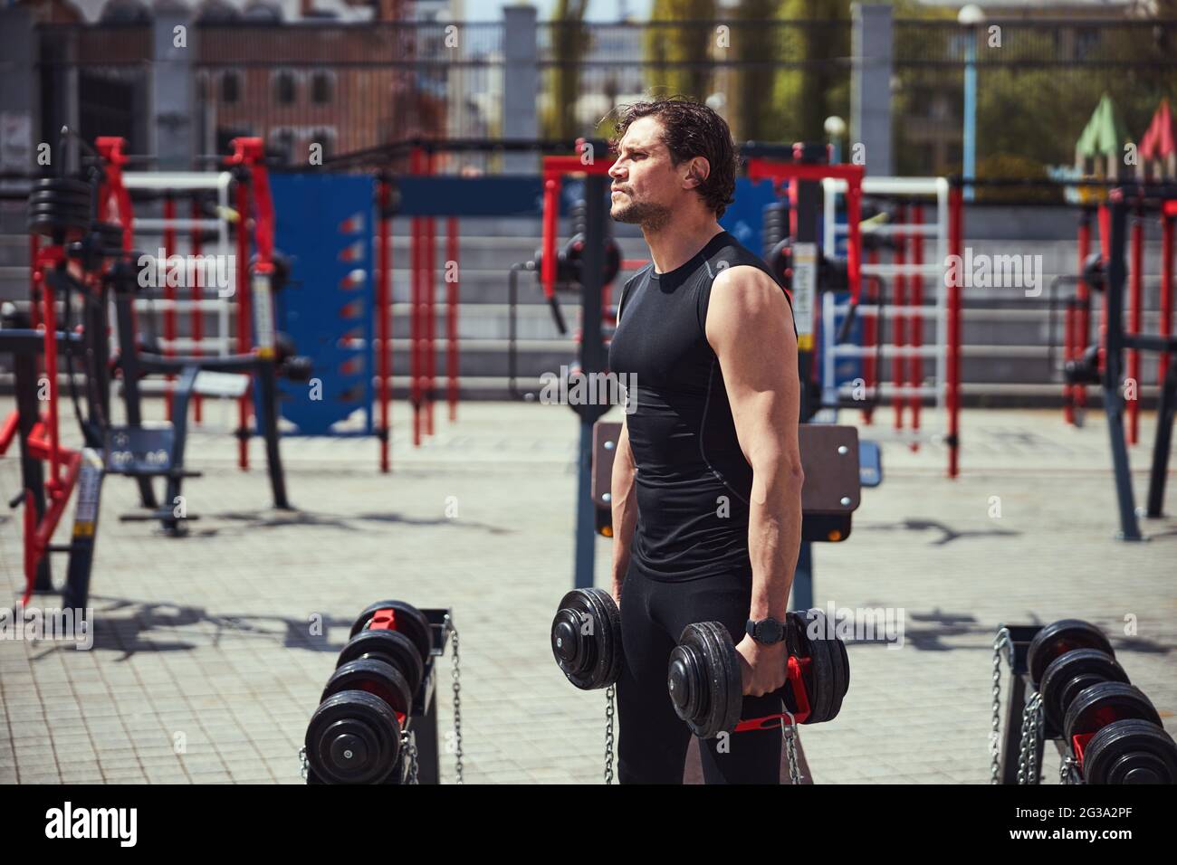 Strong male lifting heavy dumbbells on sports ground Stock Photo - Alamy