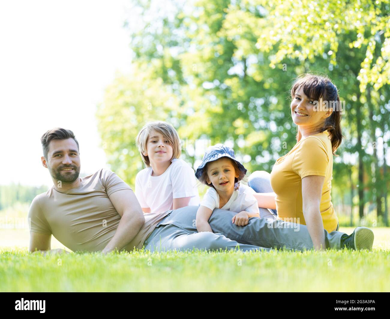 Portrait of happy family of parents and two children sitting in park ...