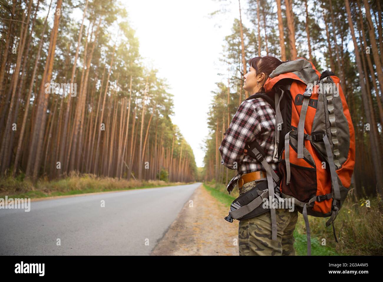 Tired female tourist walking on the roadside with big backpack ...