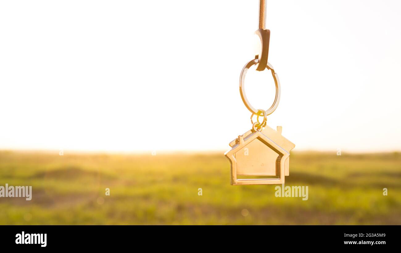House key with keychain in hand. Background of sky, sunlight and field ...