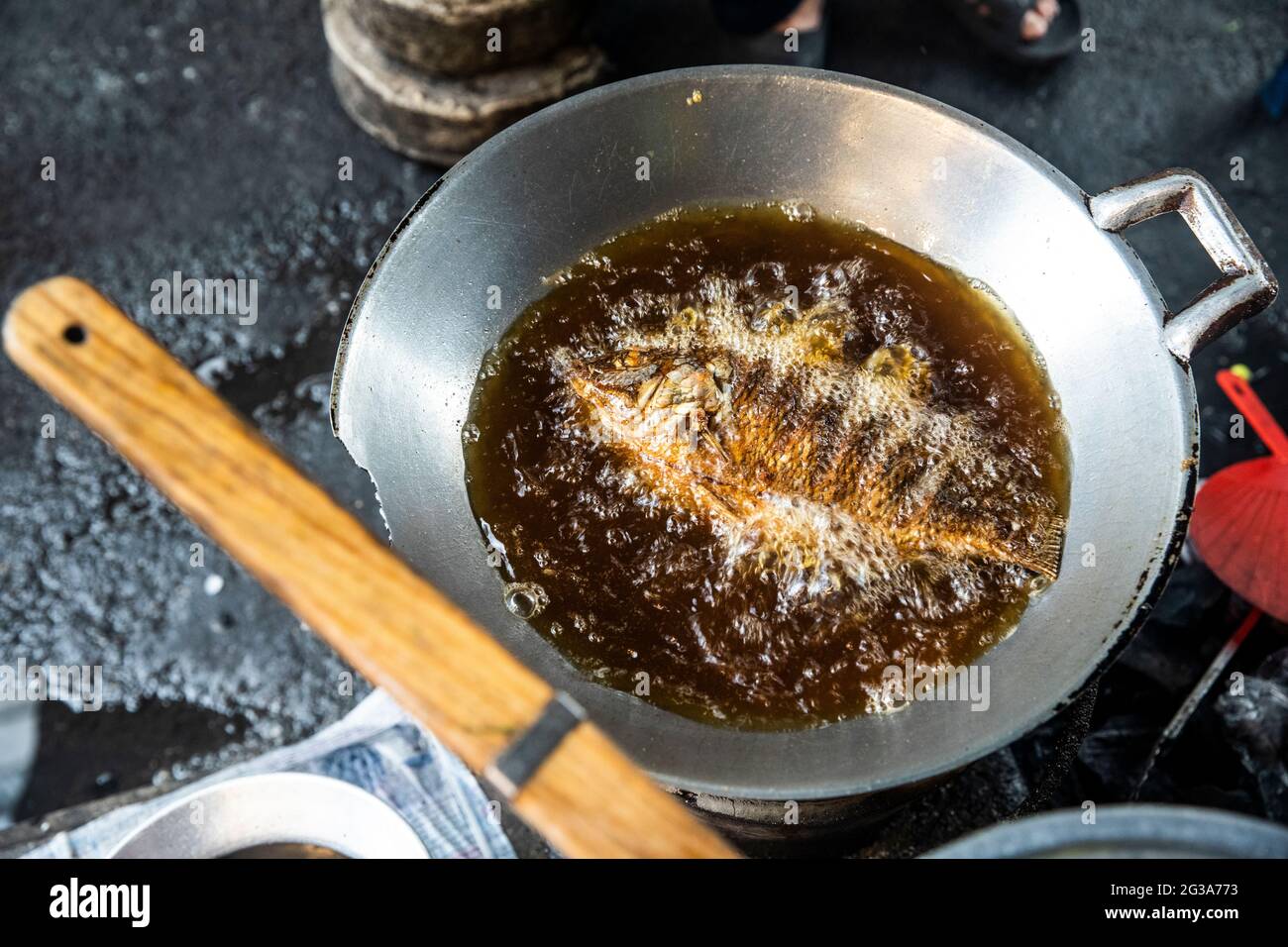 A whole fish is fried in oil at a street food kiosk in the Bang Rak ...