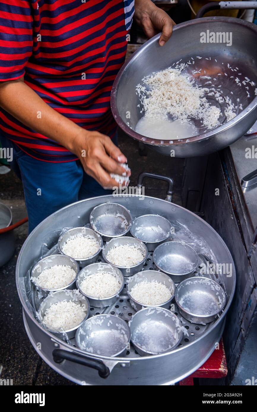 A Thai street food vendor prepares rice to be cooked into a popular ...