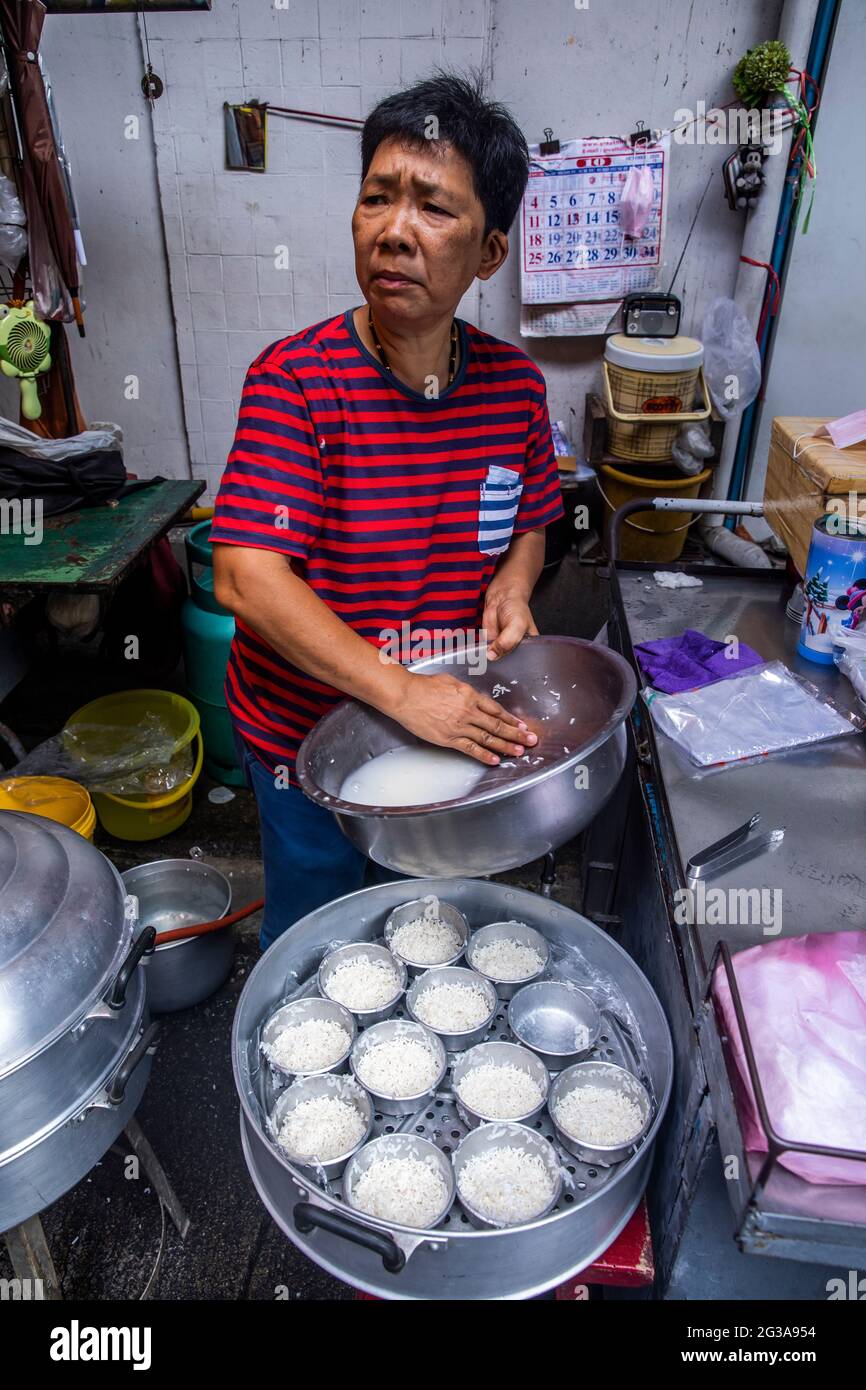 A Thai street food vendor prepares rice to be cooked into a popular ...