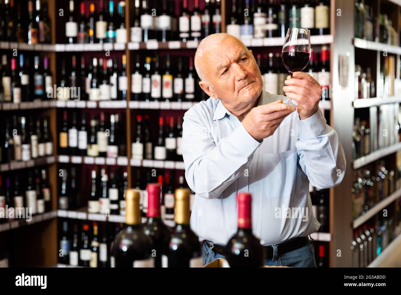 Elderly man checks the color and taste of red wine in a liquor store ...