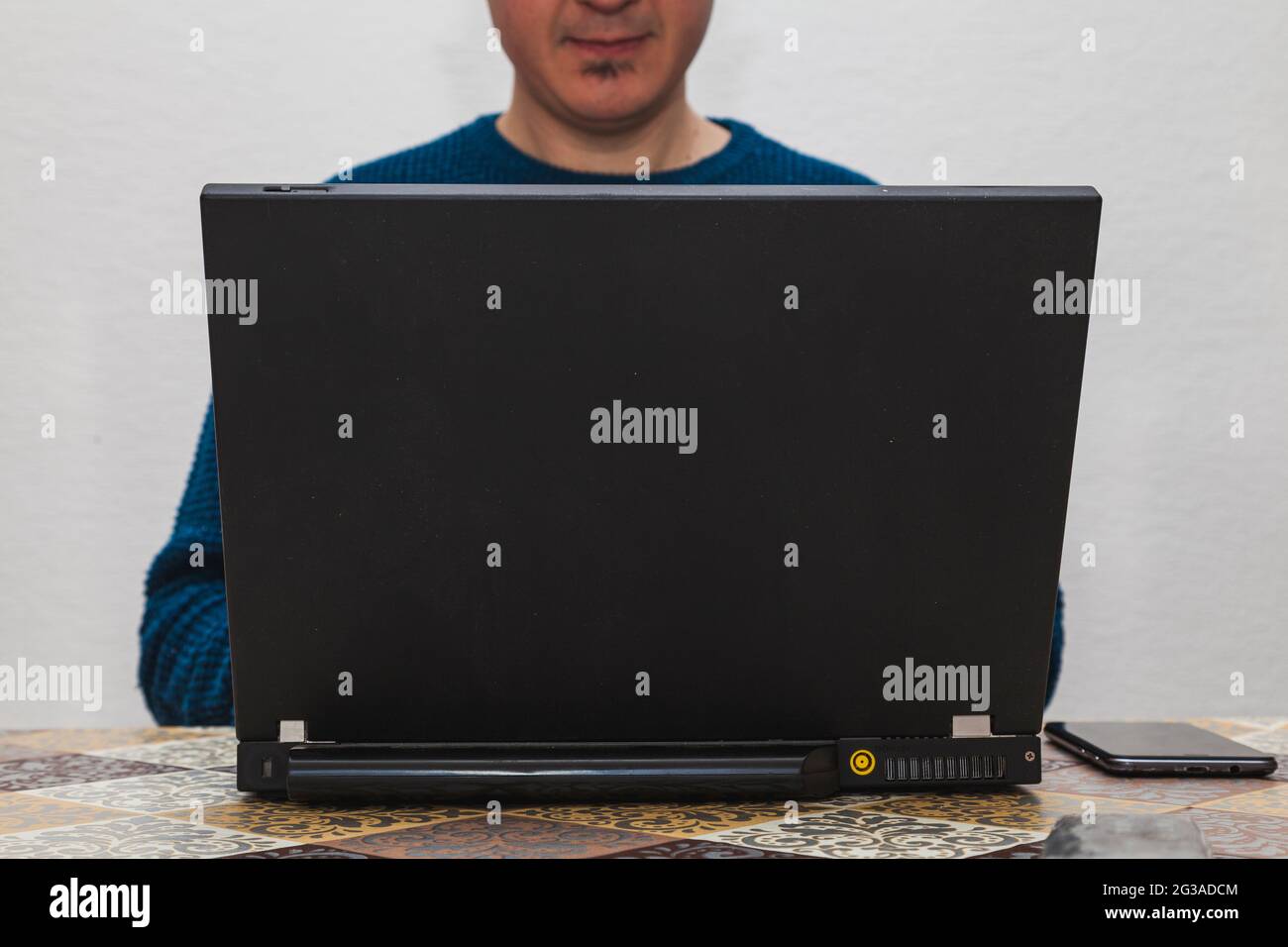 An unknown man in a blue sweater is typing on a laptop. He can't see ...