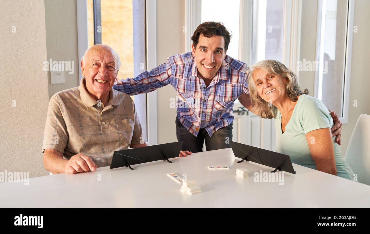 Happy senior couple and son playing rummikub at home or retirement home ...
