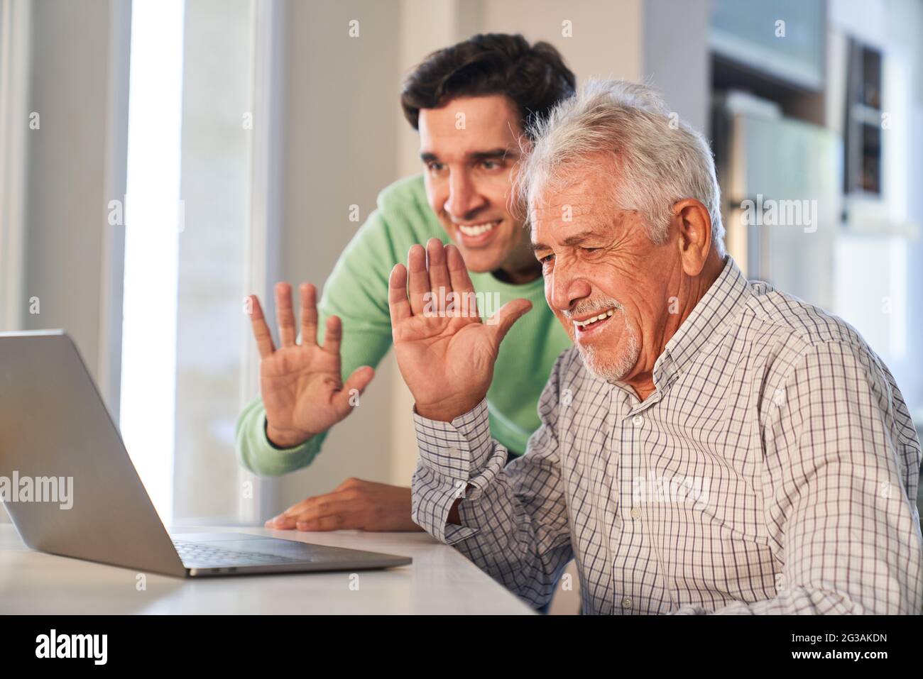 Senior and young man waving while streaming video with family on laptop ...