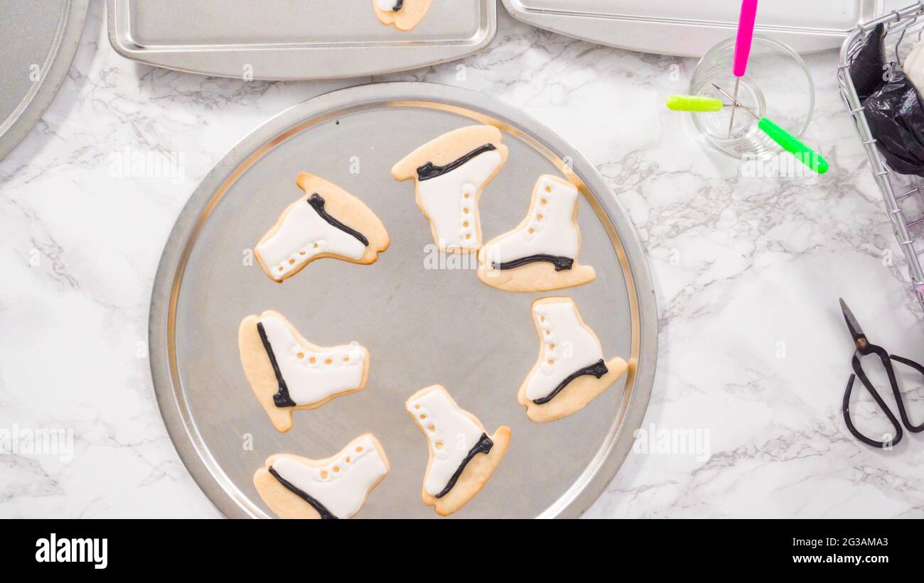 Flat lay. Decorating ice skate shaped sugar cookies with black color ...