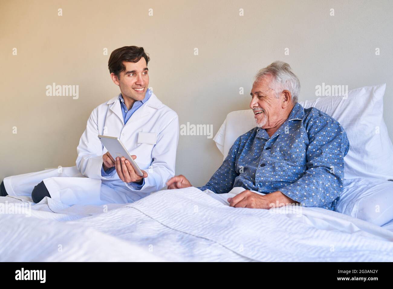 Male nurse shows his tablet computer to senior patient in bed in the ...
