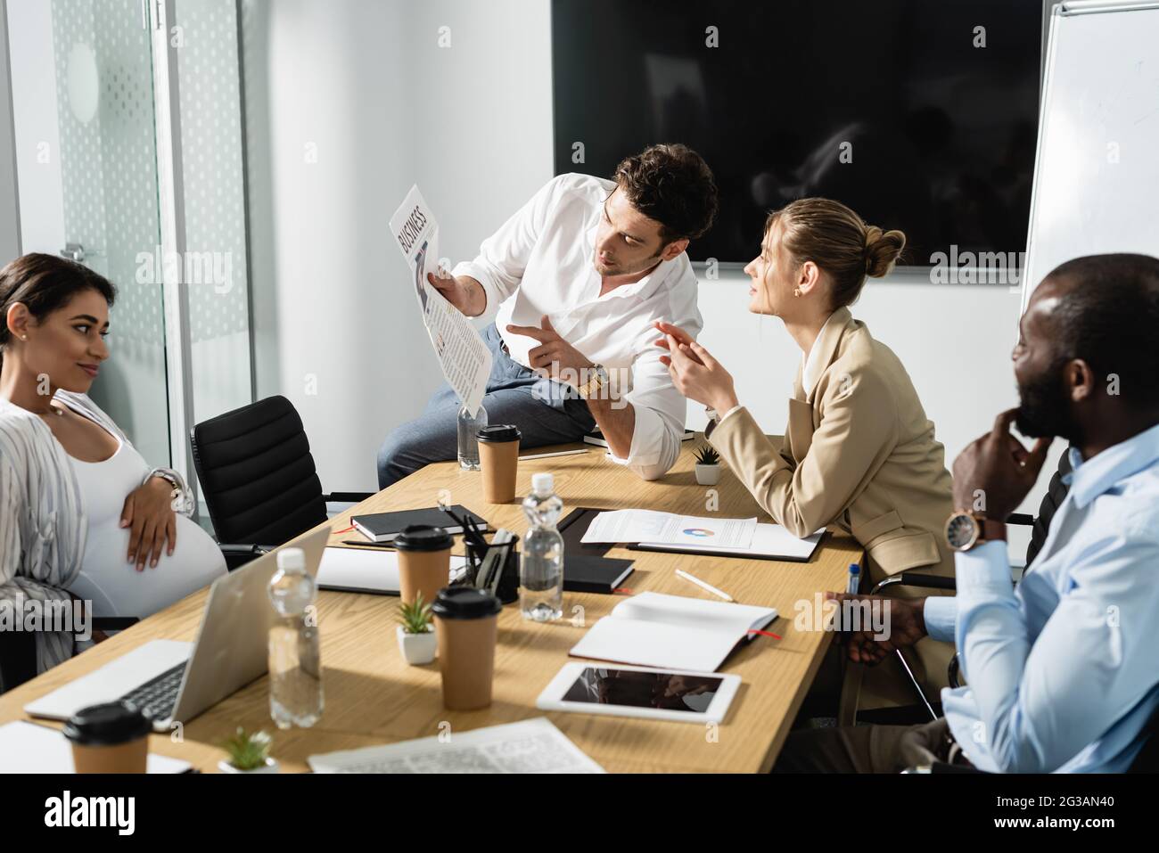 businessman pointing at article in newspaper during meeting with ...