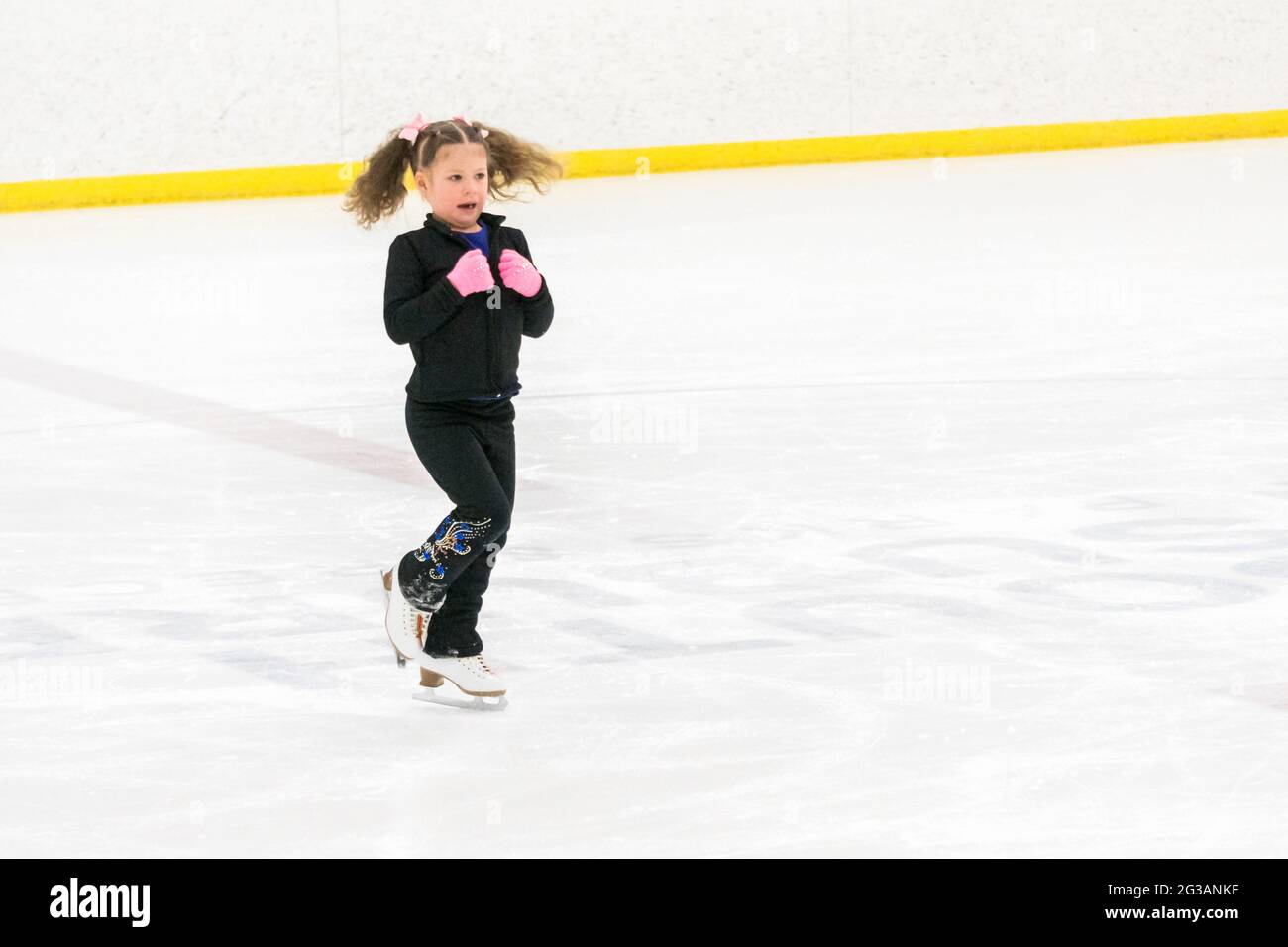 Little girl practicing figure skating moves on the indoor ice rink ...