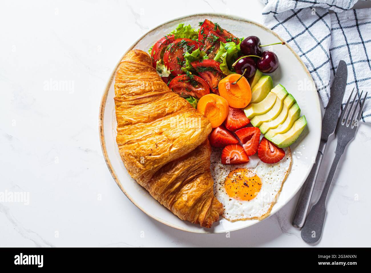 Breakfast plate with croissant, avocado, fried egg, salad and fruit ...