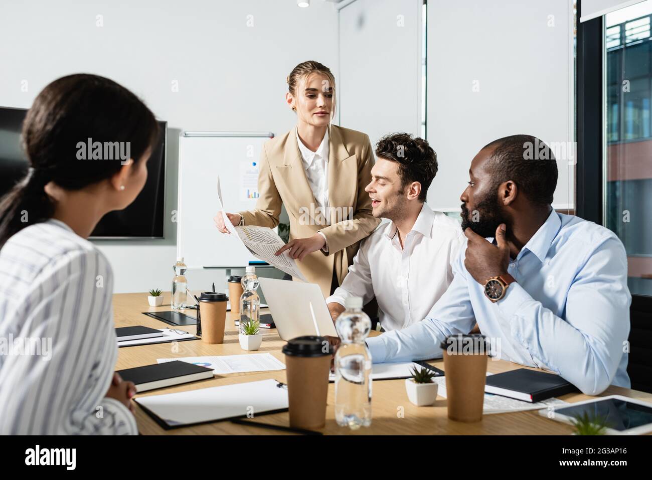 businesswoman pointing at newspaper near amazed multiethnic colleagues ...