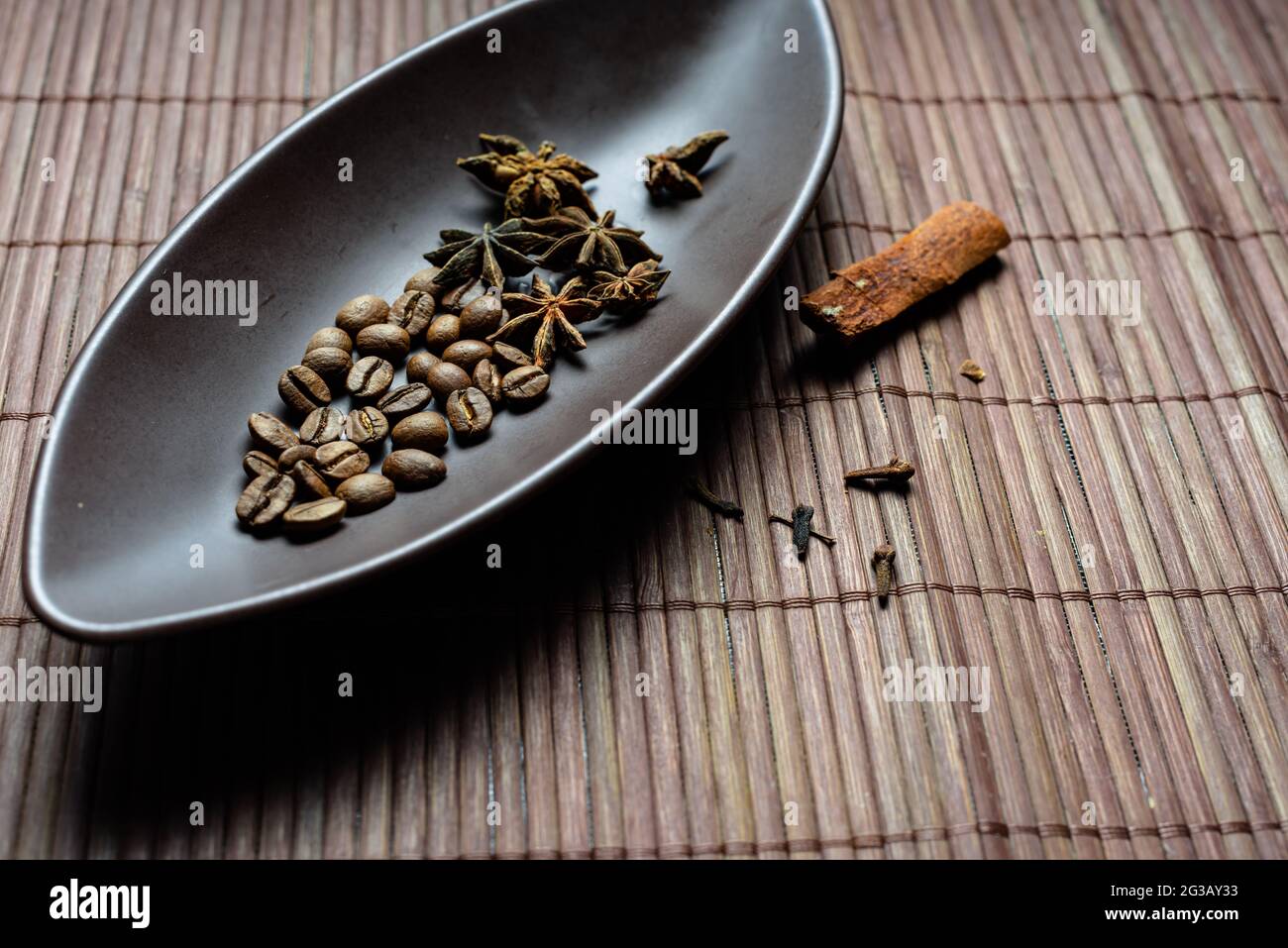 Brown canoe-shaped dish on bamboo mat with coffee beans, star anise ...