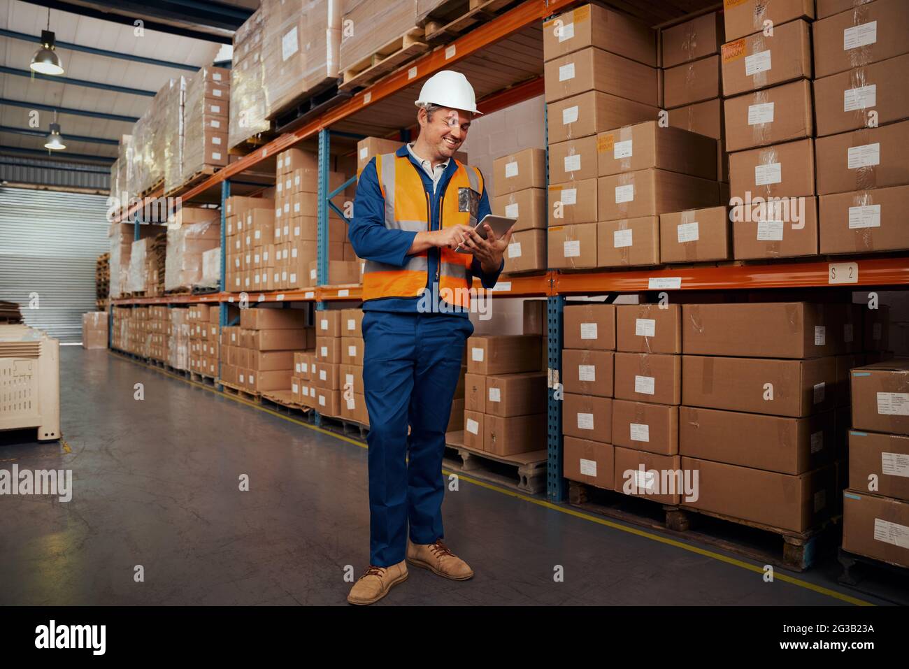 Cheerful male warehouse supervisor standing in warehouse using smart ...