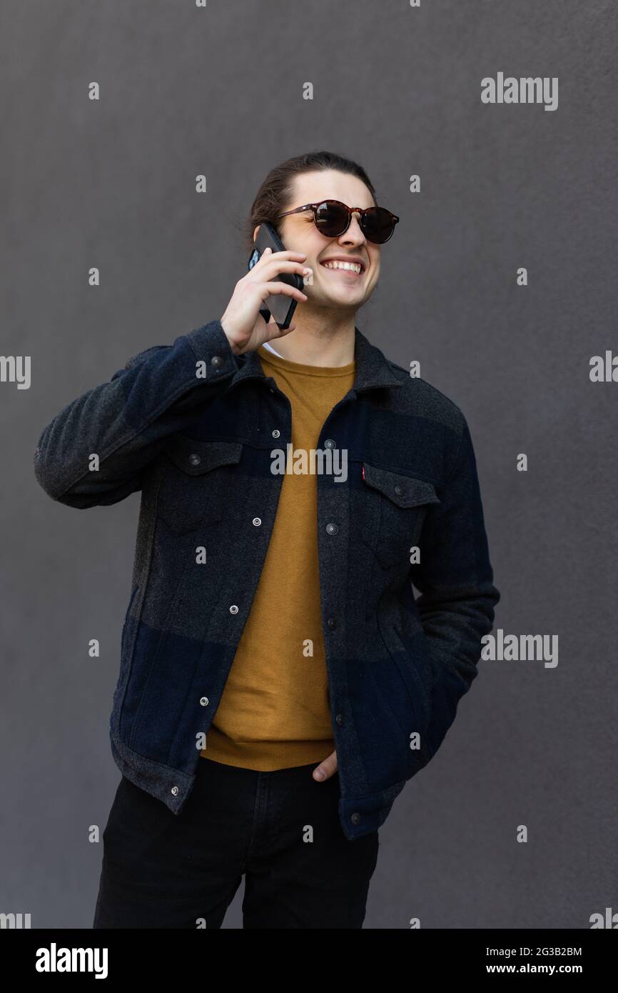 Portrait of handsome male student walking outdoors on university campus and talking on mobile ...