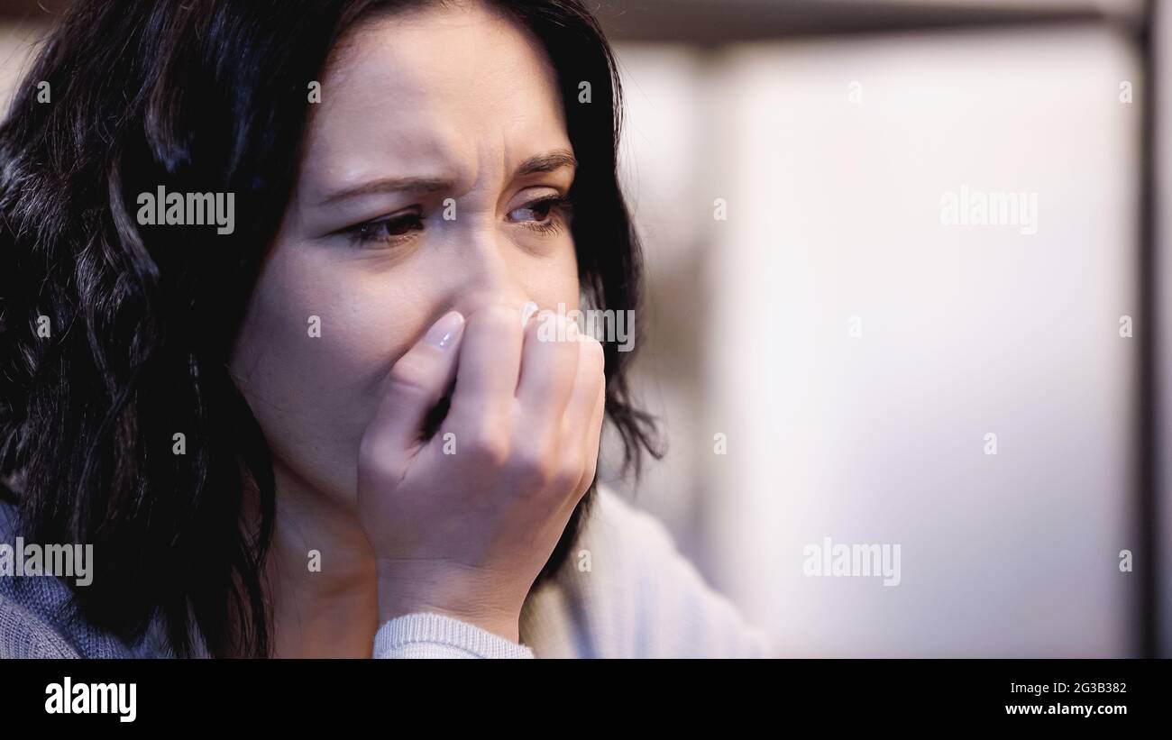portrait of upset brunette woman crying and covering mouth with hand at ...