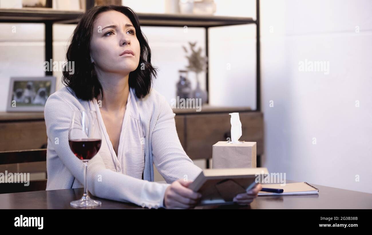 upset woman sitting on table with photo frame in hands and crying with ...