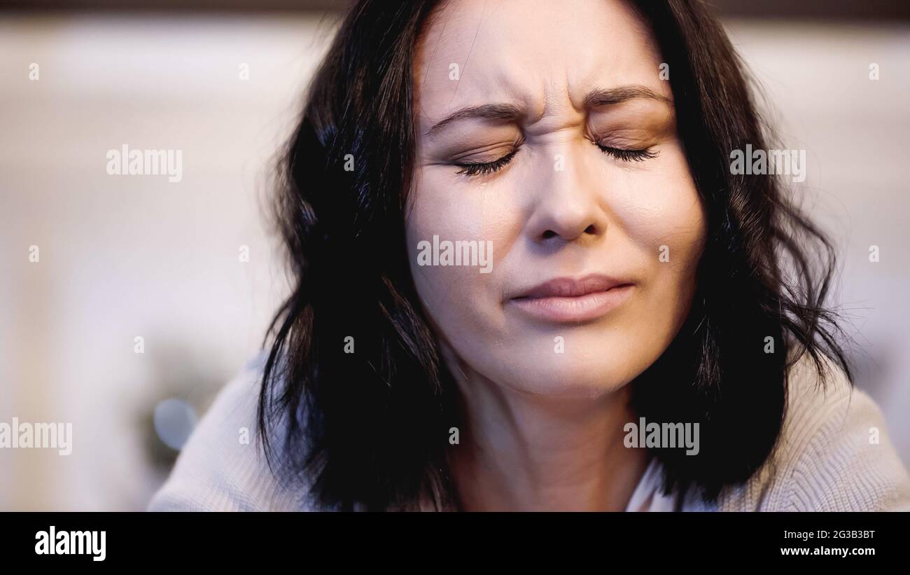 portrait of crying brunette woman with closed eyes on beige background ...