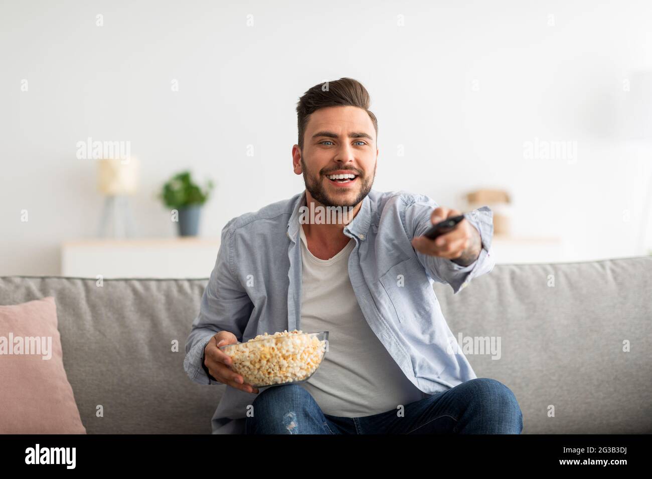 Domestic pastime. Cheerful man resting on couch switching channels with ...