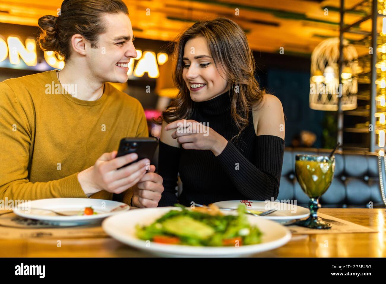 Cheerful couple browsing internet on smartphone during romantic dinner ...