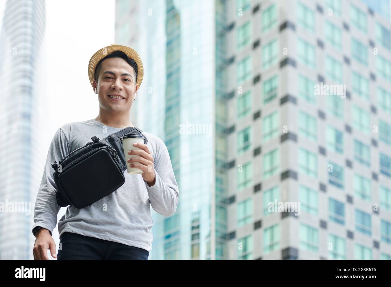 Portrait of happy young Asian guy in straw hat holding takeout coffee ...